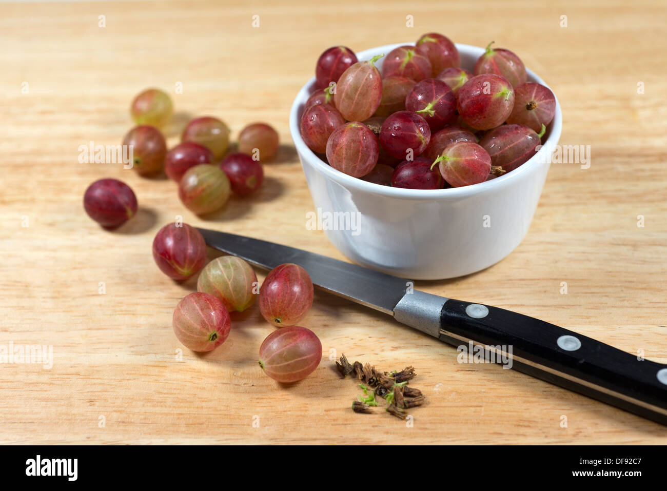 Small white bowl of red gooseberries being topped and tailed ready to ...