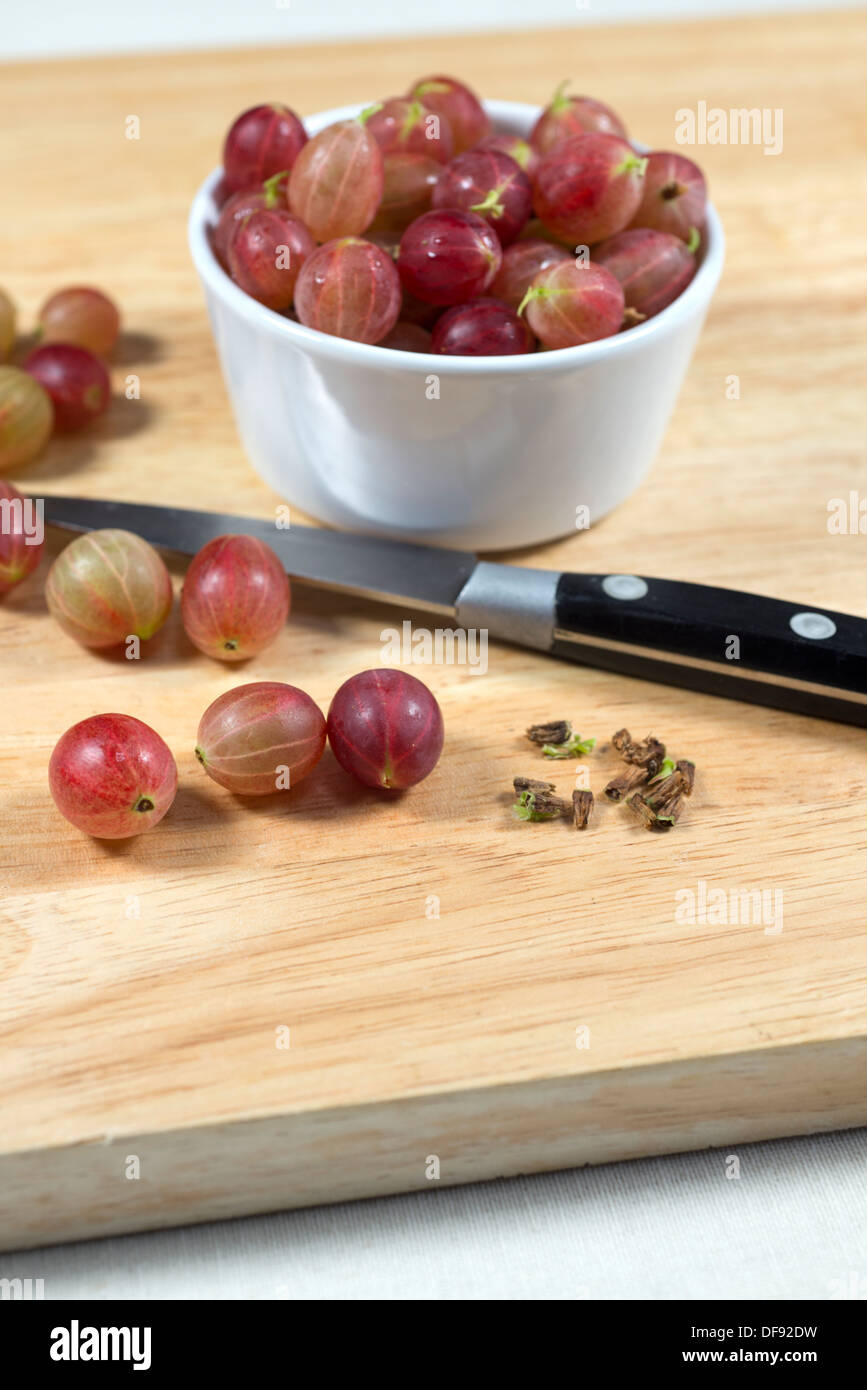 Small white bowl of red gooseberries being topped and tailed ready to ...