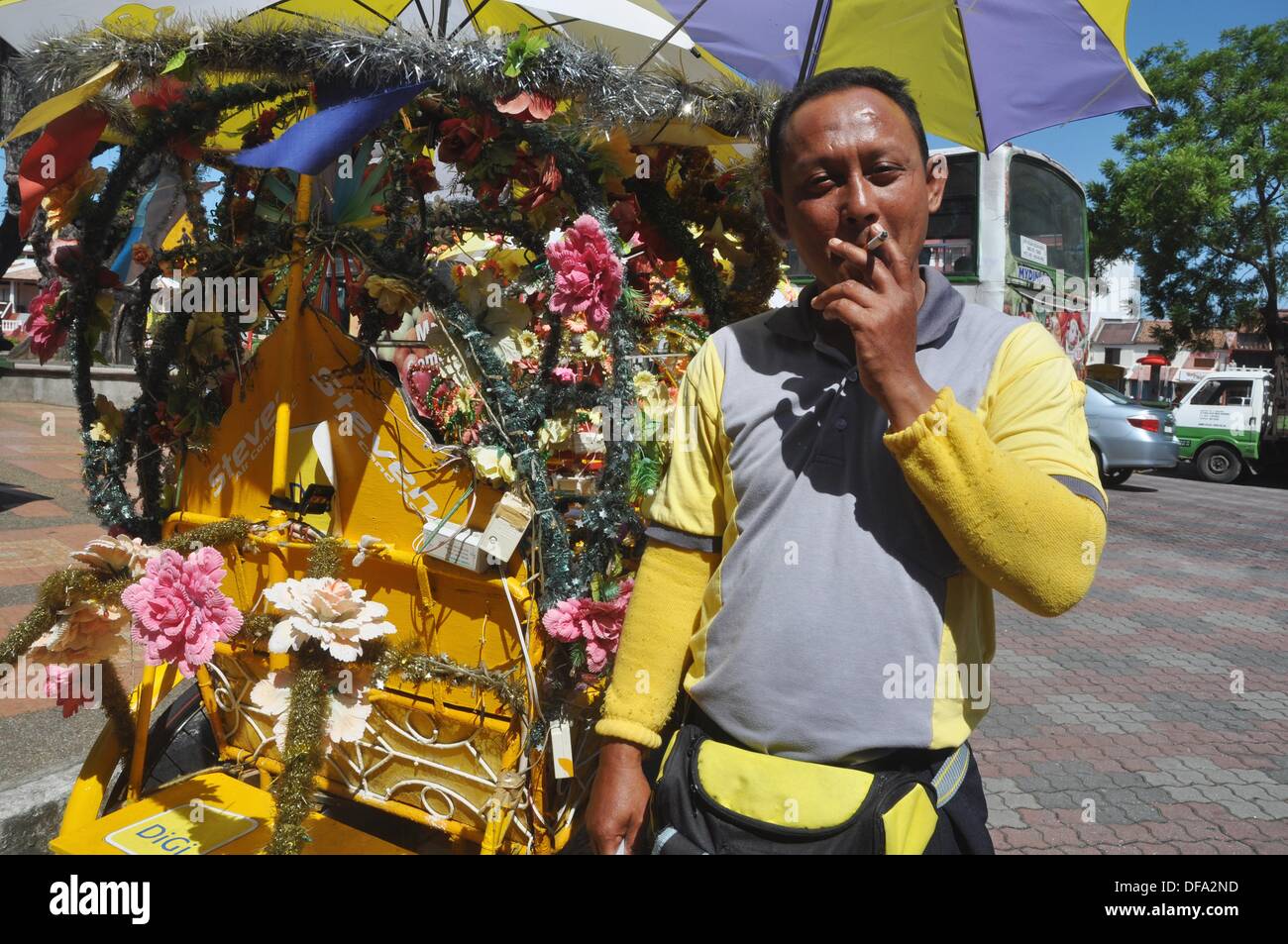 Malacca (Malaysia): a rickshaw driver, smoking a cigarette during a ...