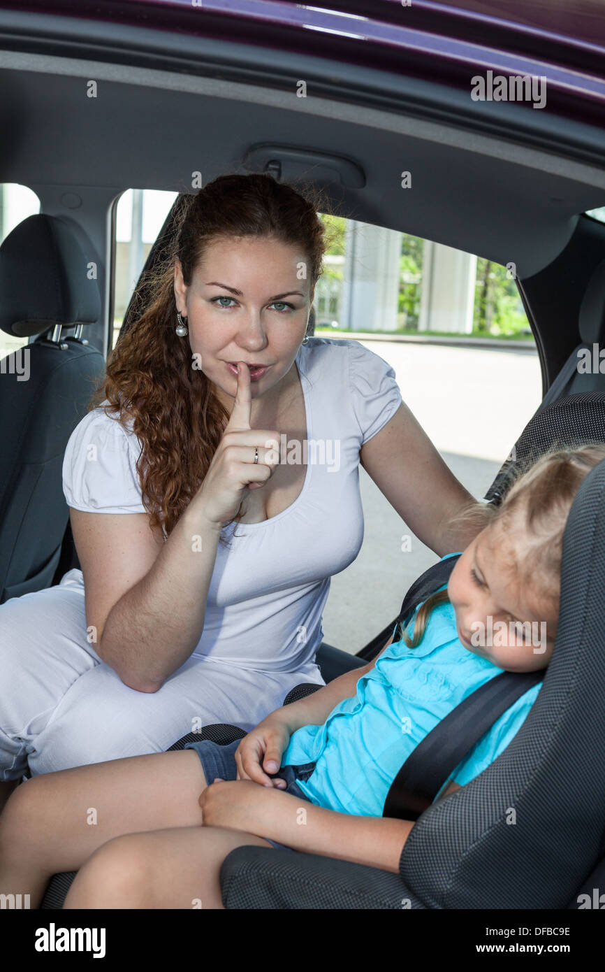 Mother showing shh gesture when daughter asleep in car safety seat ...
