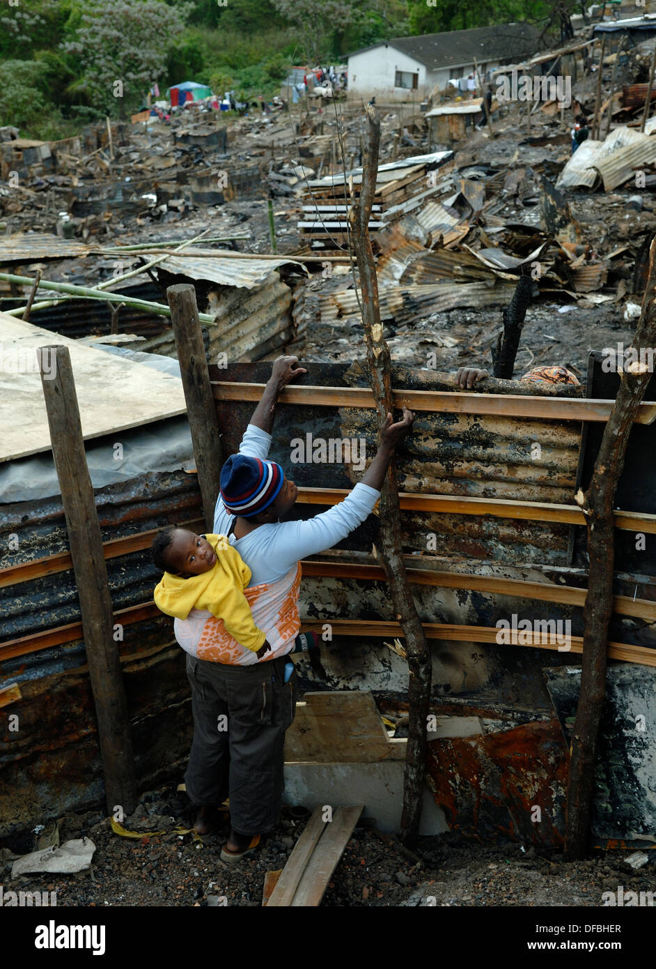 A woman with her child on her back rebuilds her shack which was ...