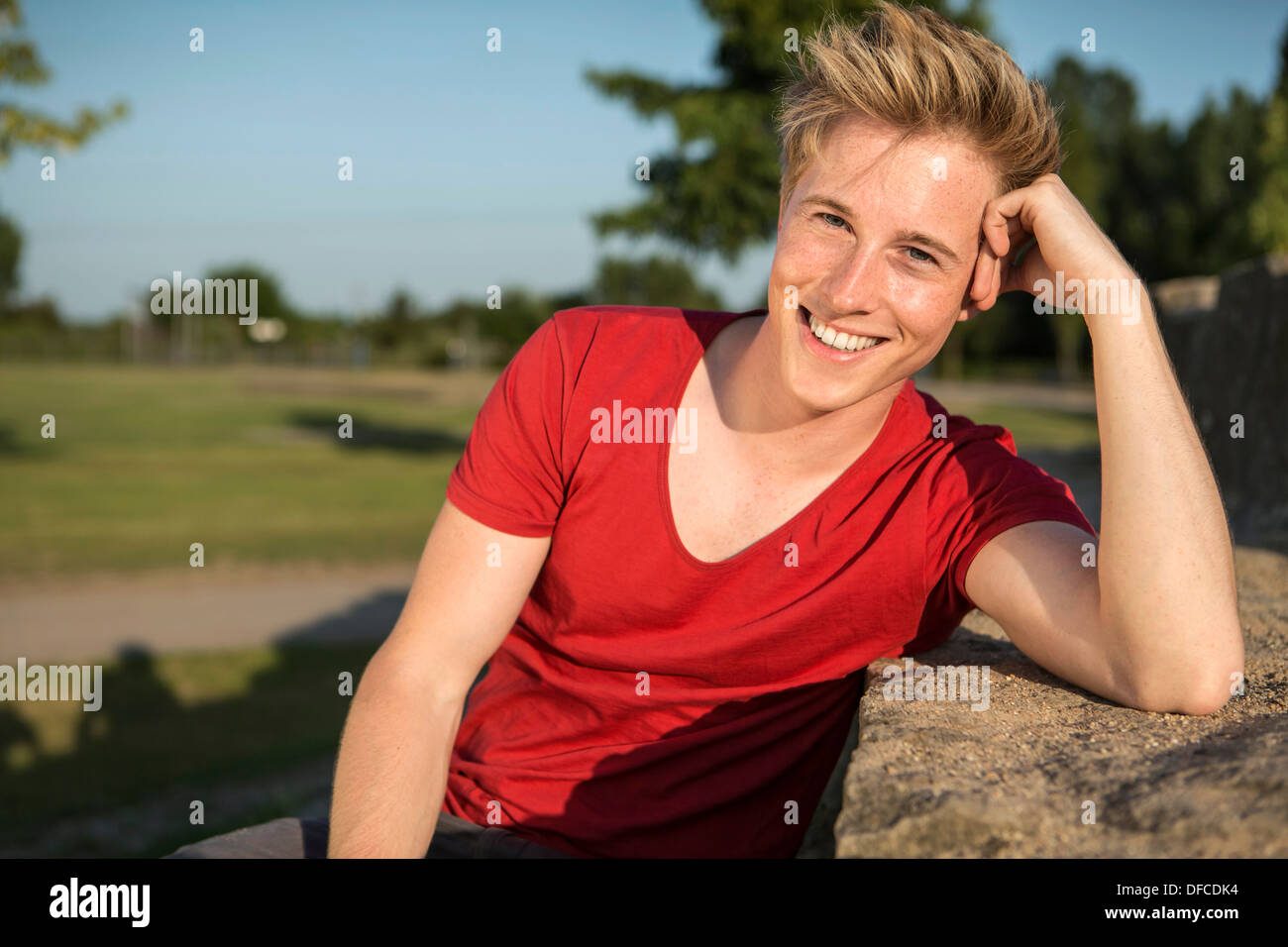 Germany, Young man sitting in park, smiling Stock Photo - Alamy