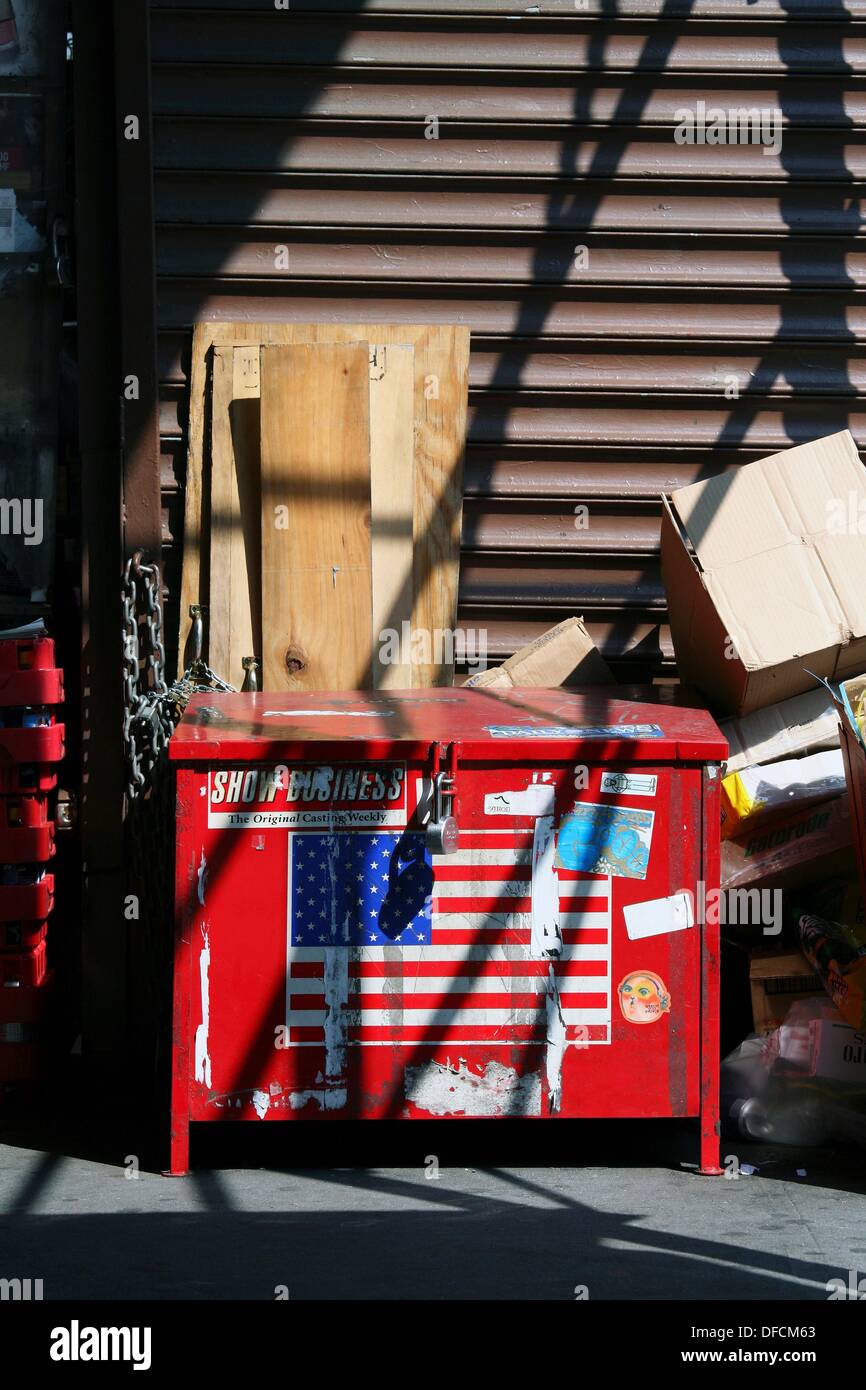 A red garbage dumpster with American flag stands on pavement covered ...
