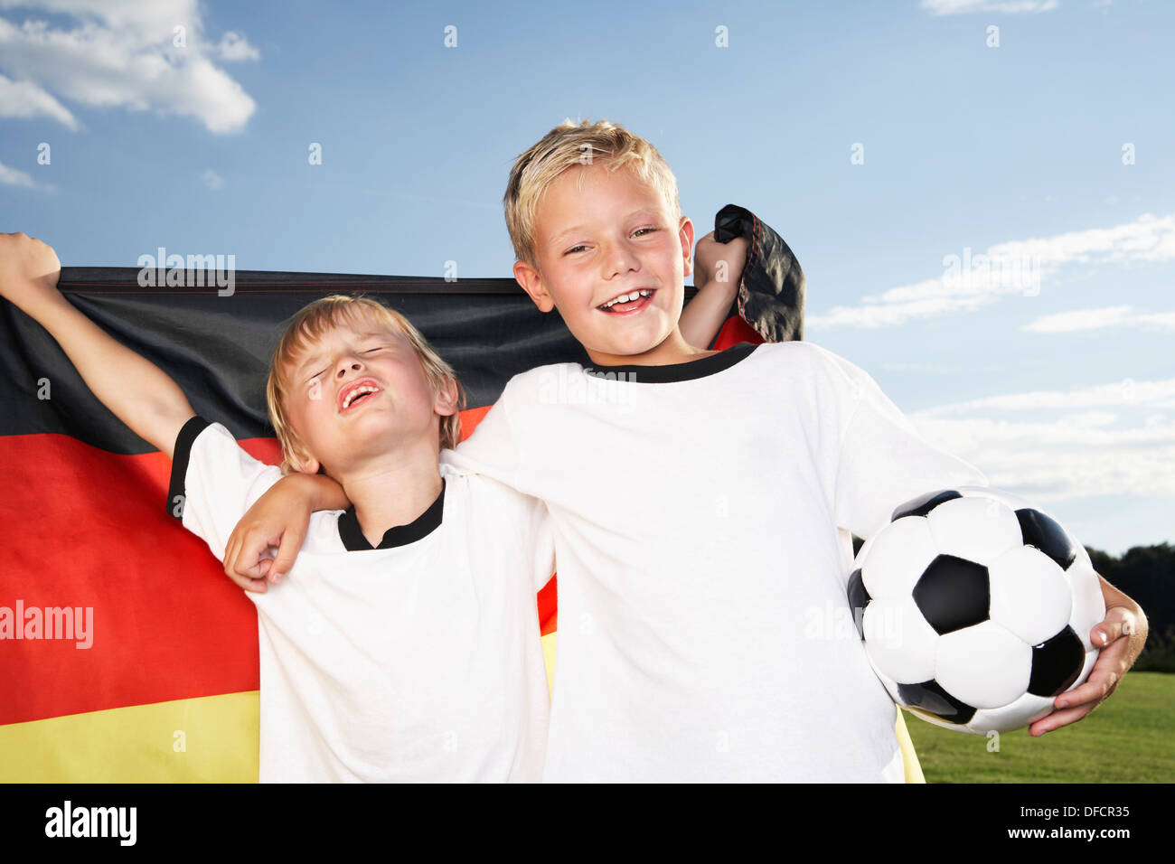 Germany, Cologne, Two boys wearing football shirts, holding German flag ...
