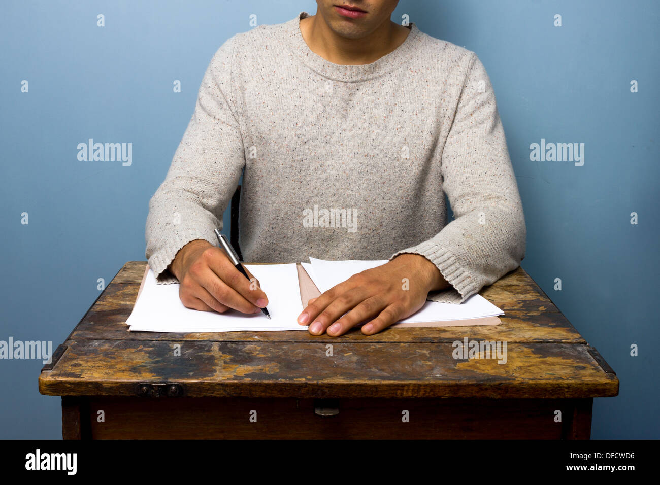 Young man is sitting at a desk and writing Stock Photo - Alamy