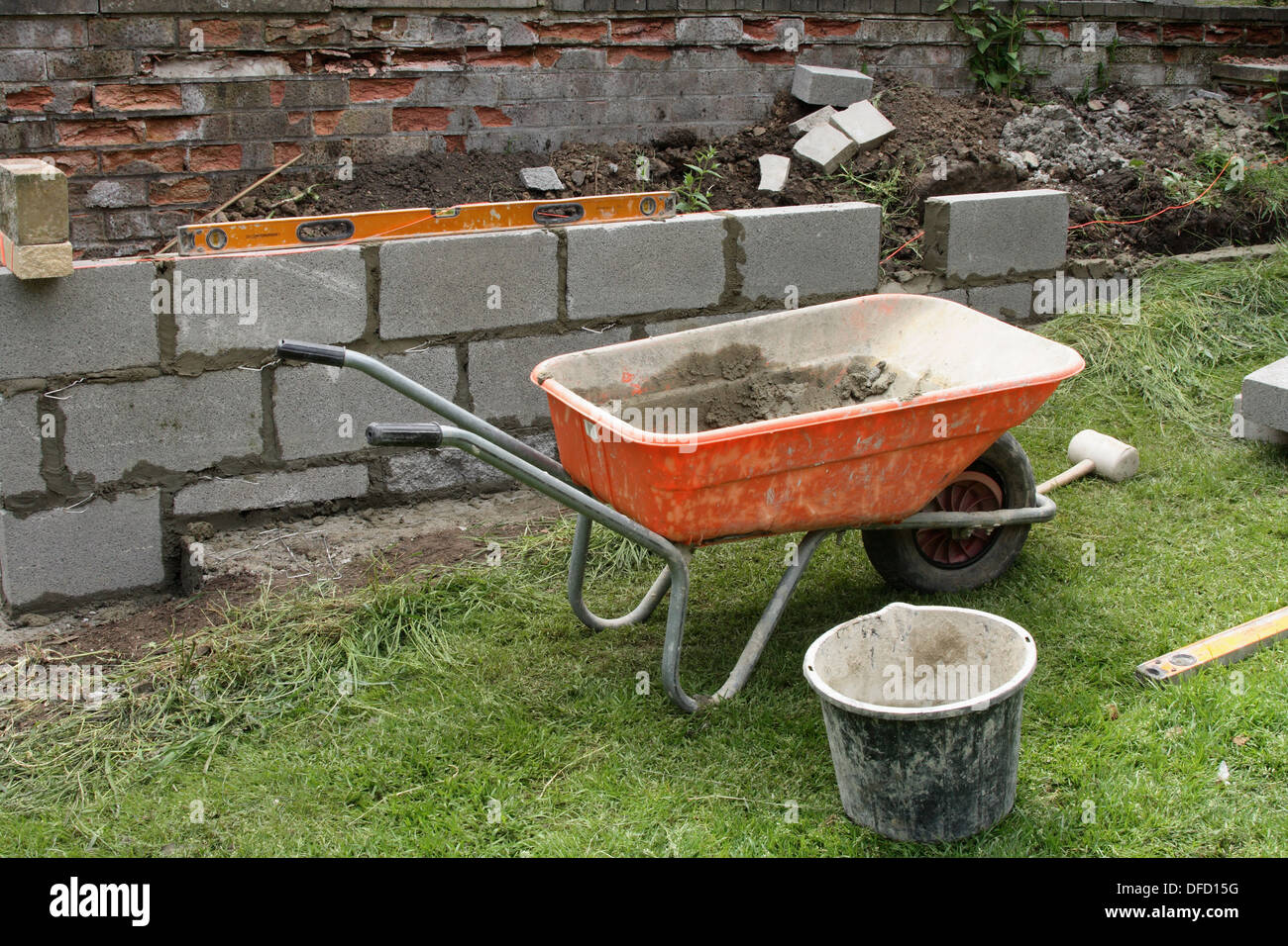 A wall is being built, a wheelbarrow full of cement is at the front of ...