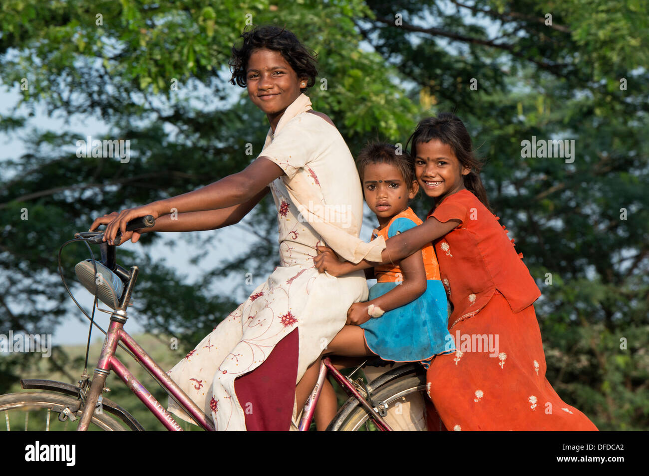 Three poor Indian village children riding a bicycle. Andhra Pradesh ...