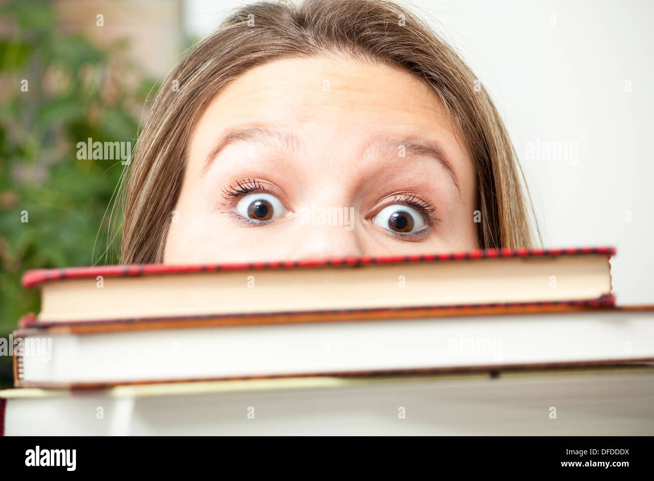 A young college student peeks up over a big stack of books in panic ...