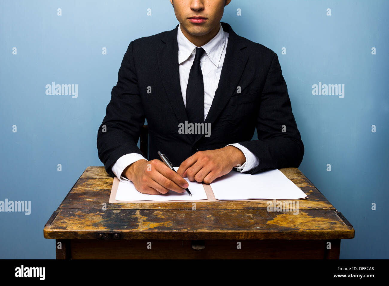 Young businessman is sitting at an old desk and signing a contract ...