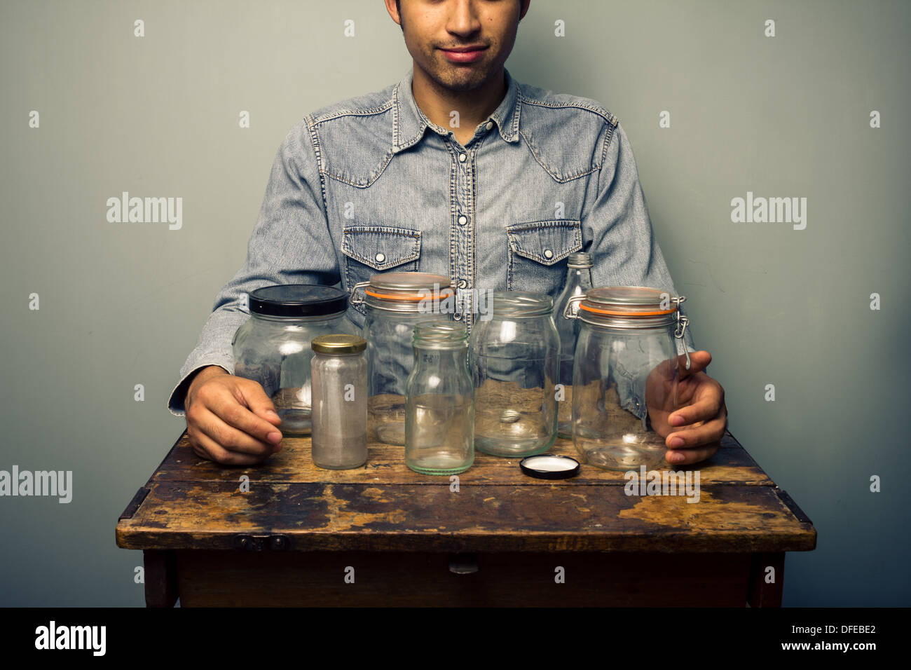 Young man is sitting at an old desk with a bunch of jam jars and empty ...