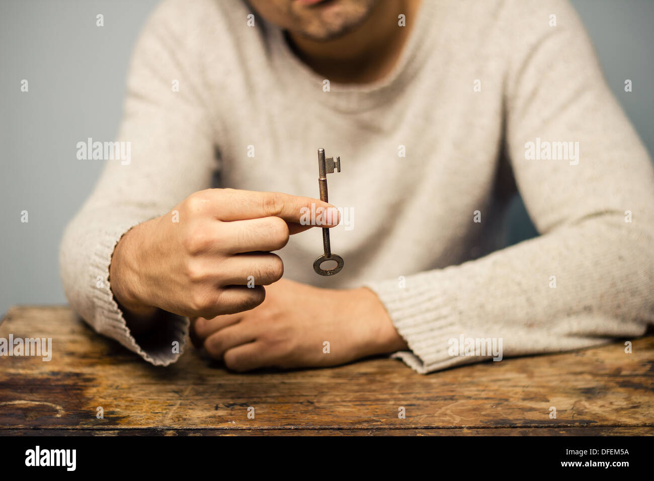 Young man is sitting at a desk and holding a key Stock Photo - Alamy