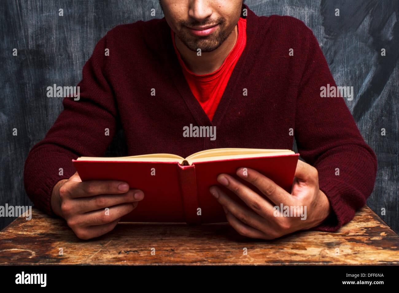 Young man is sitting in front of a blackboard and reading a book Stock ...