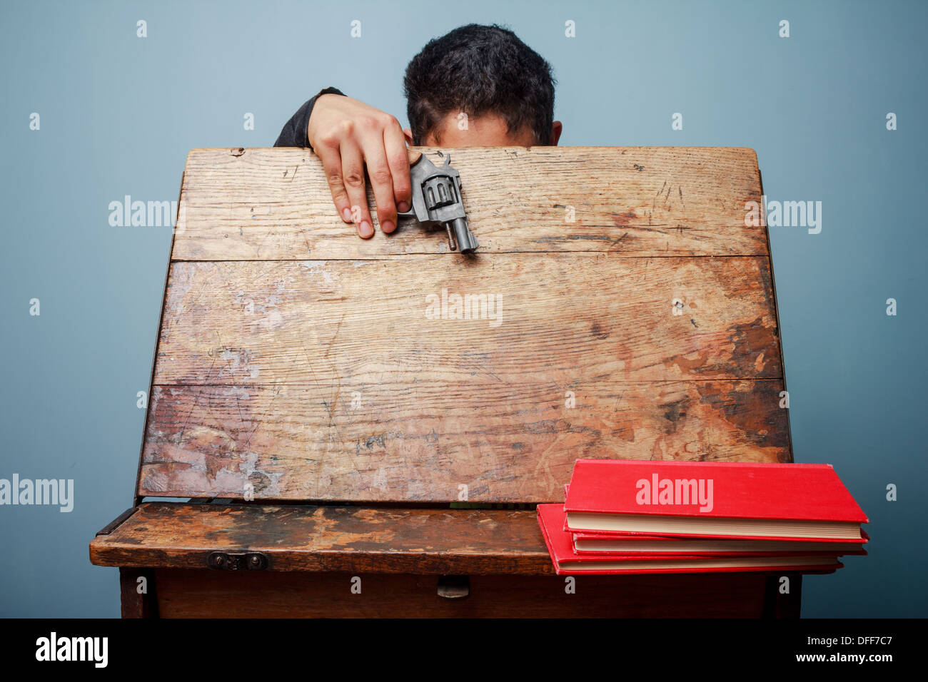 Student sitting at old school desk holding a gun, there's a stack of ...