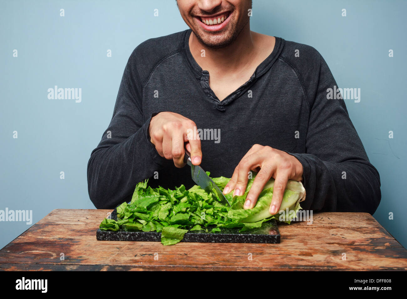 Smiling young man chopping lettuce at a table Stock Photo - Alamy