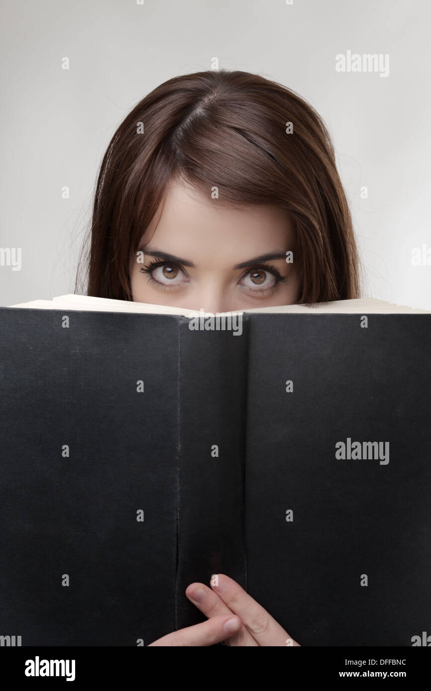 just woman eyes peering over a hard back book Stock Photo - Alamy