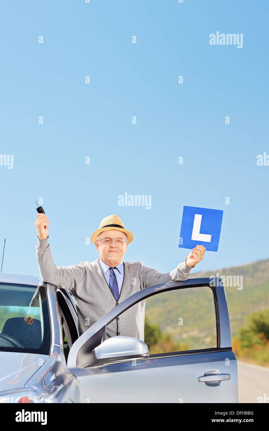 Happy mature man next to car holding a L sign and car key after having ...