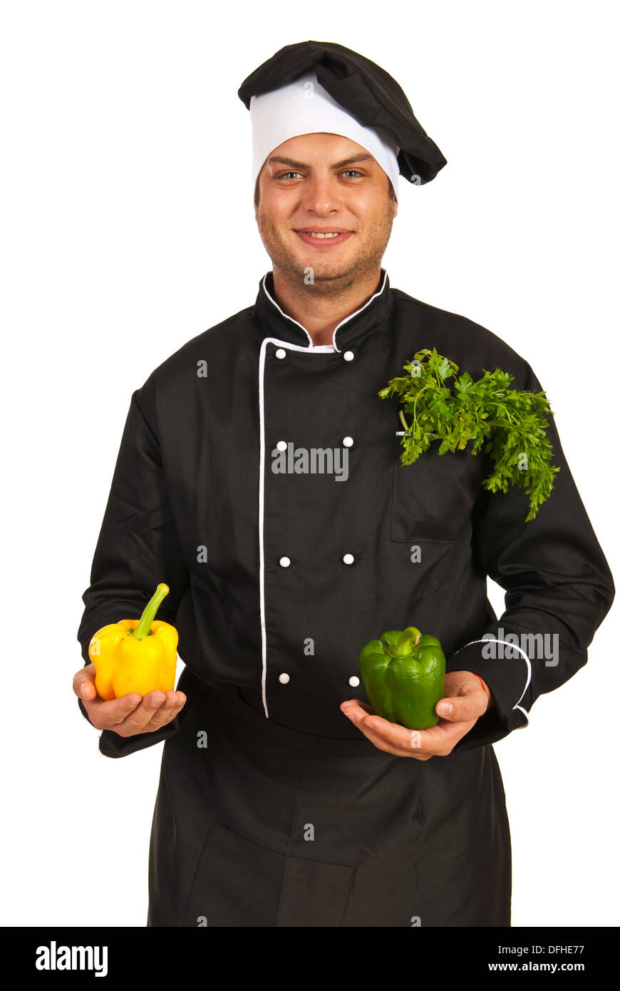 Cheerful chef with parsley in uniform pocket showing bell peppers ...
