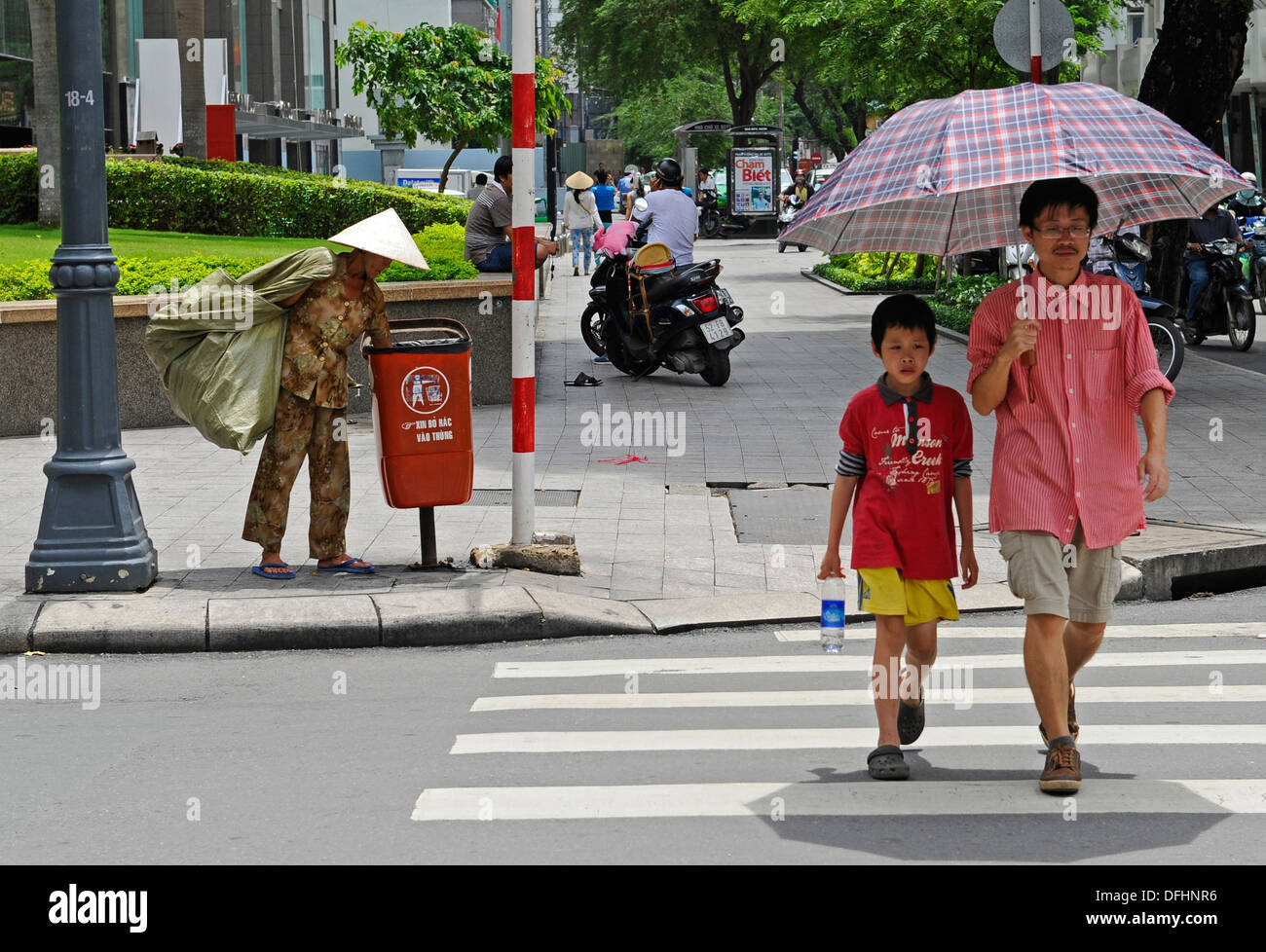 Female rubbish collector emptying a road side bin whilst man and boy ...