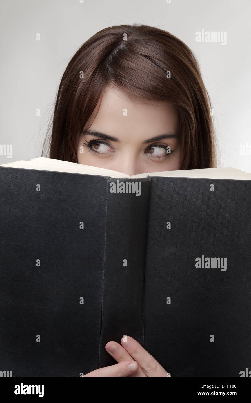 just woman eyes peering over a hard back book Stock Photo - Alamy