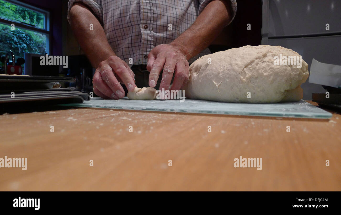 Front view of man's hands shaping bread dough rolls at kitchen counter ...