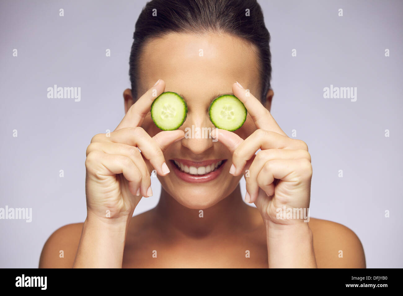 Beautiful and smiling young woman holding slice of cucumber in front of ...