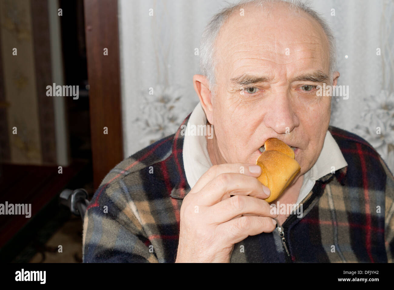 Elderly pensive man eating a freshly baked bread roll staring ...