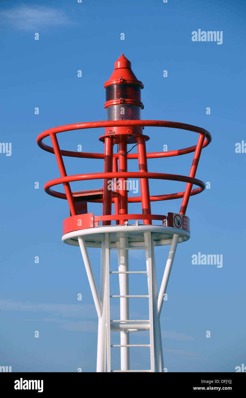 A red and white light beacon against blue sky in the harbour of ...