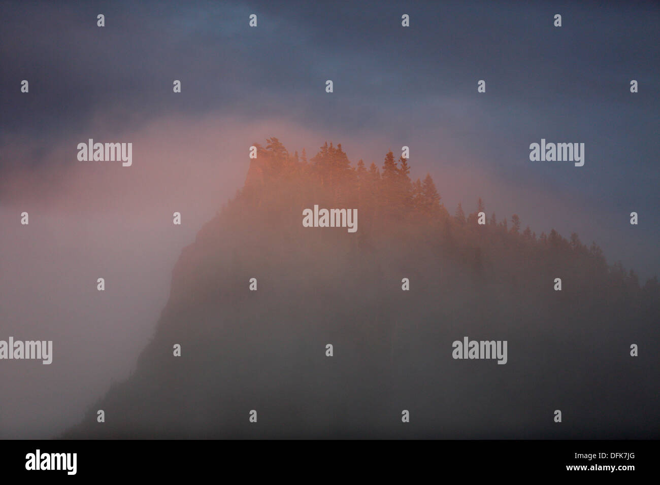 The setting sun illuminates a fog shrouded ridge, Percé, Québec, Canada ...