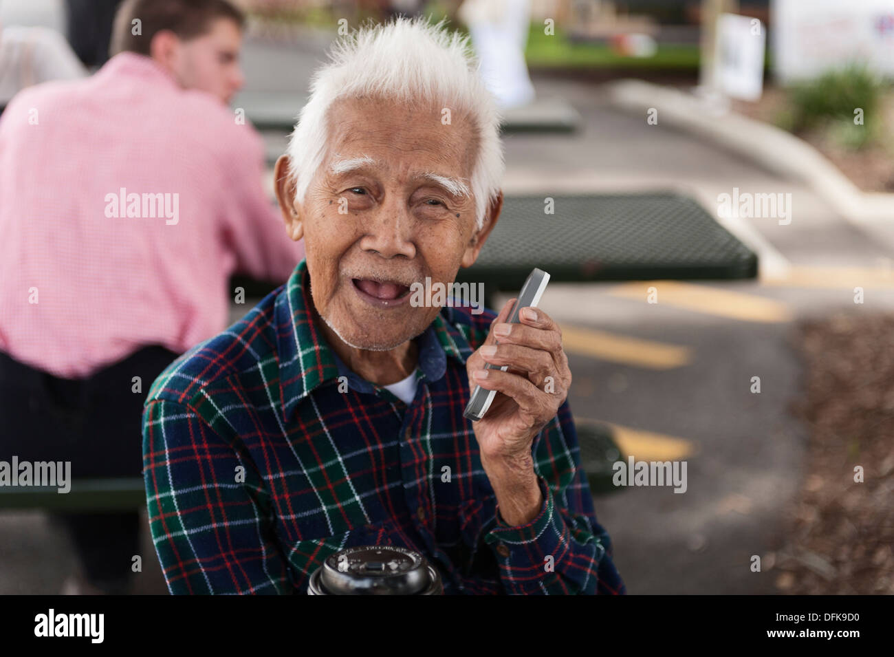 A Senior citizen man with no teeth holding a smart phone close to his ...