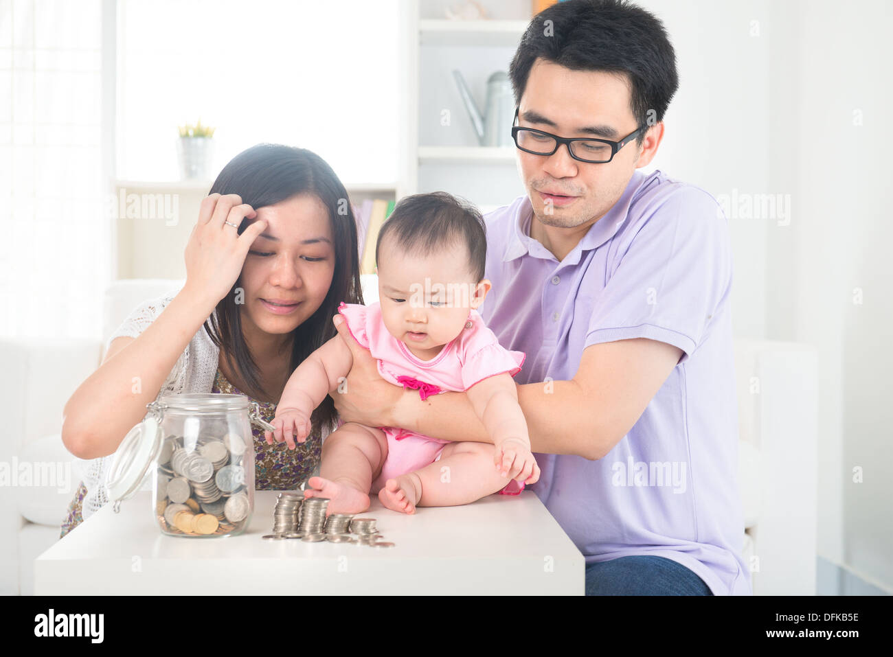 Asian baby putting coins into the glass bottle with help of parents ...