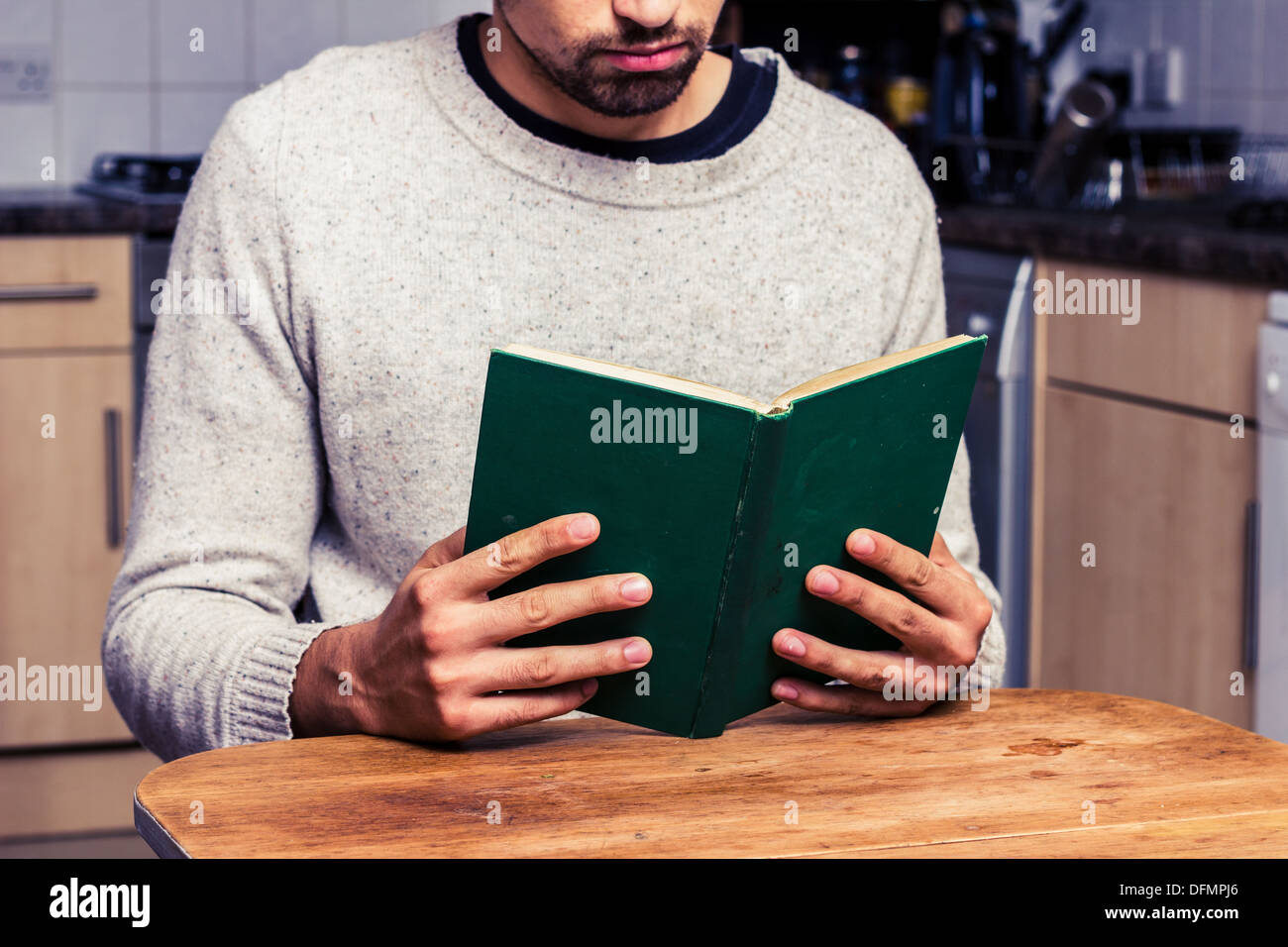 Young man reading a book in his kitchen Stock Photo - Alamy