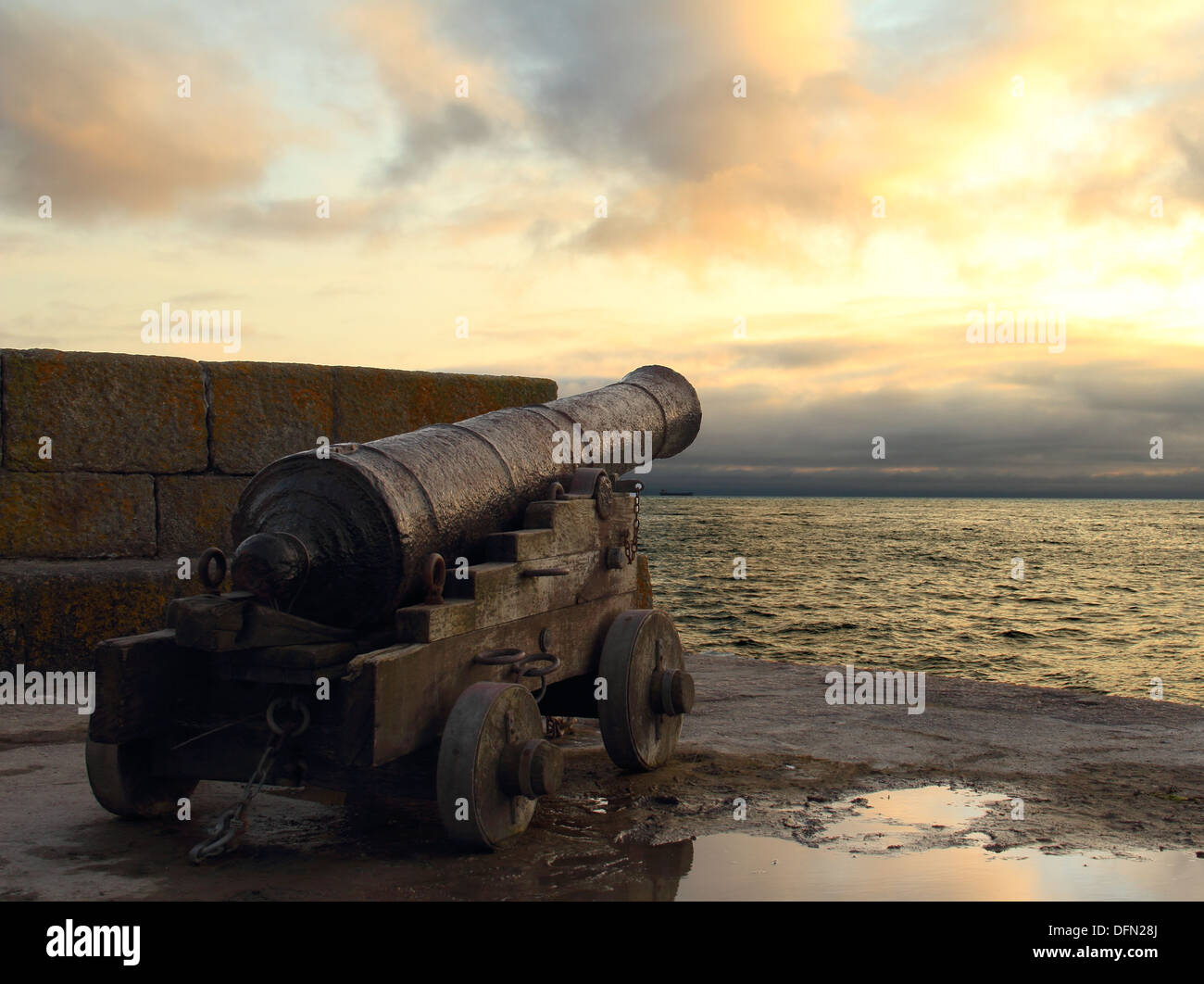 Old, rusted cannon pointing out to sea during a dramatic sunset over ...