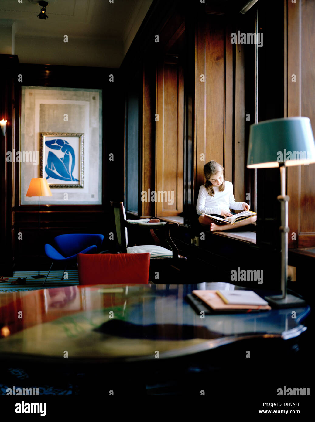 Girl reading a book while sitting on a window sill in a hotel room ...