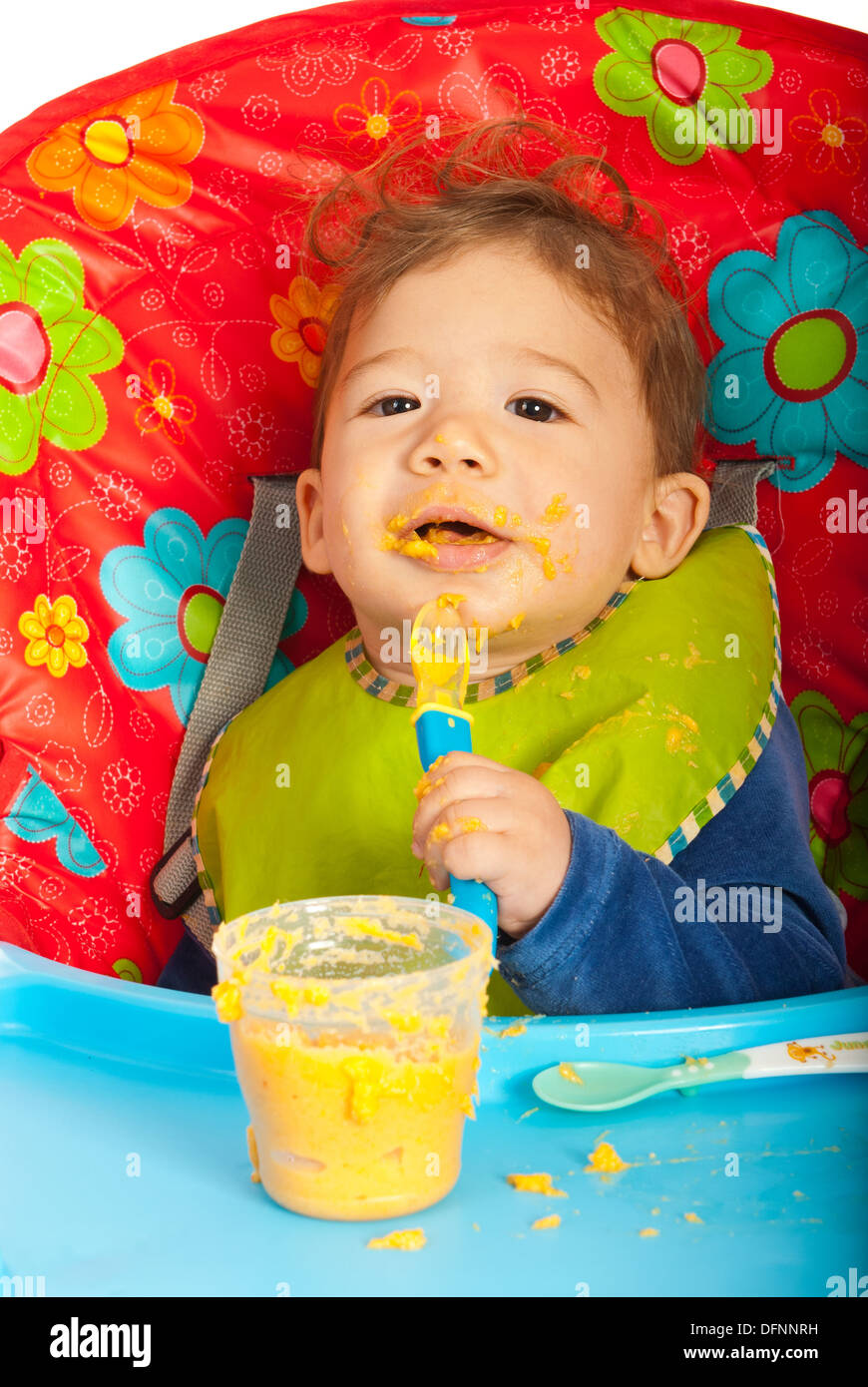 Messy baby eating puree with spoon by yourself and sitting chair Stock ...