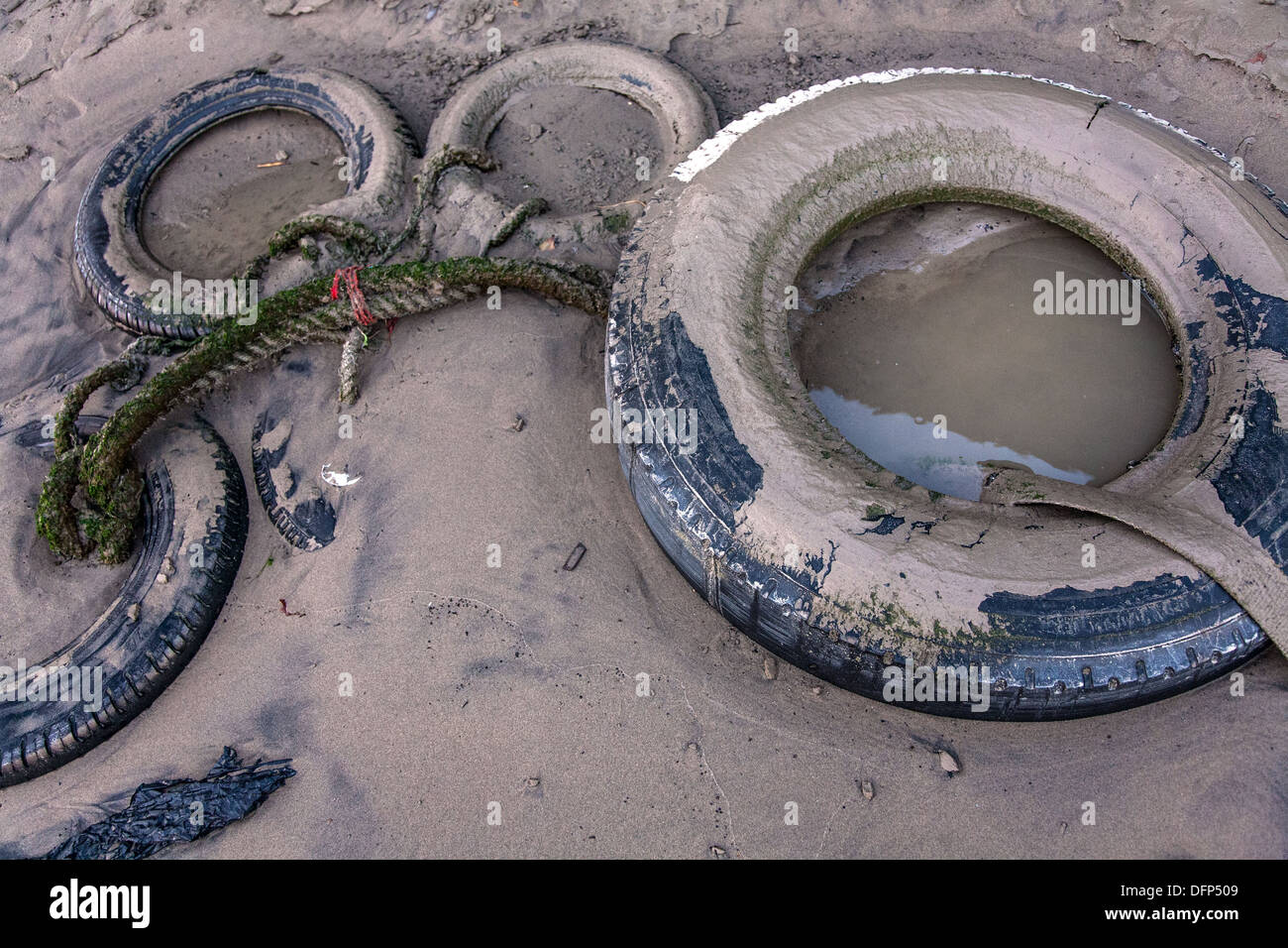 4 rubber tyres buried in the sand connected by a rope Stock Photo - Alamy