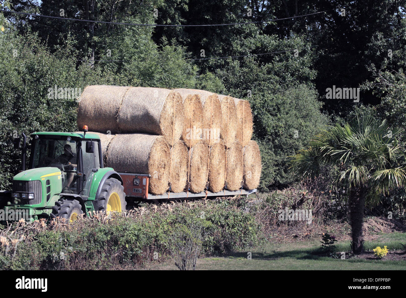 A tractor pulling a trailer loaded with bales of hay along a country ...