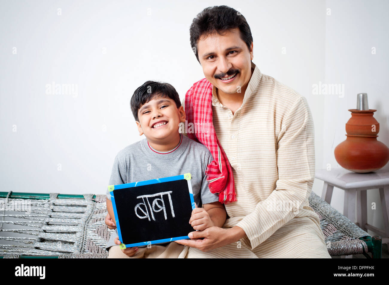 Portrait of a man sitting with his son holding a slate with word Baba ...