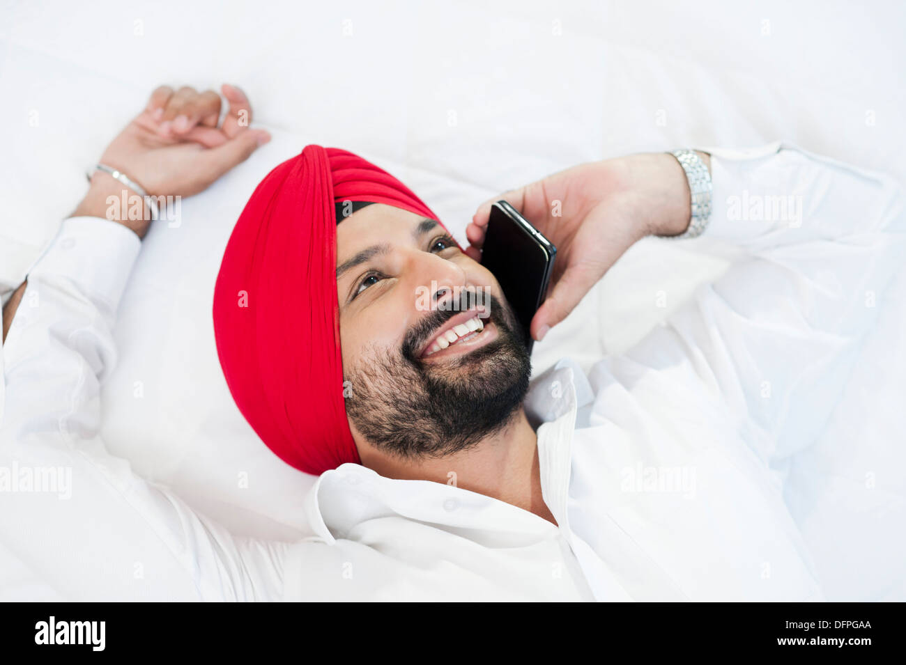 Smiling Sikh man lying on the bed and talking on mobile phone Stock ...
