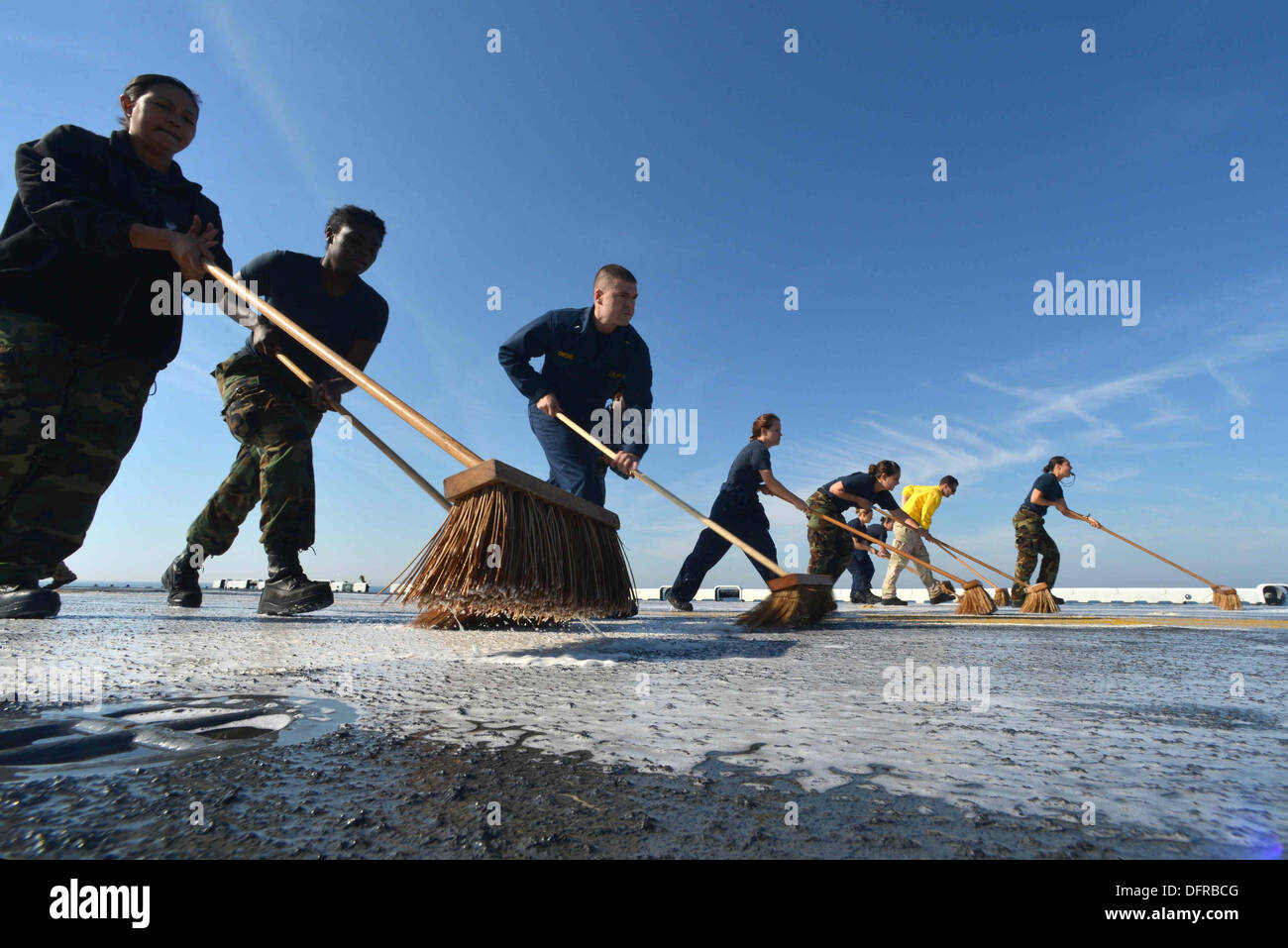 Sailors clean the flight deck with brooms during a freshwater flight ...