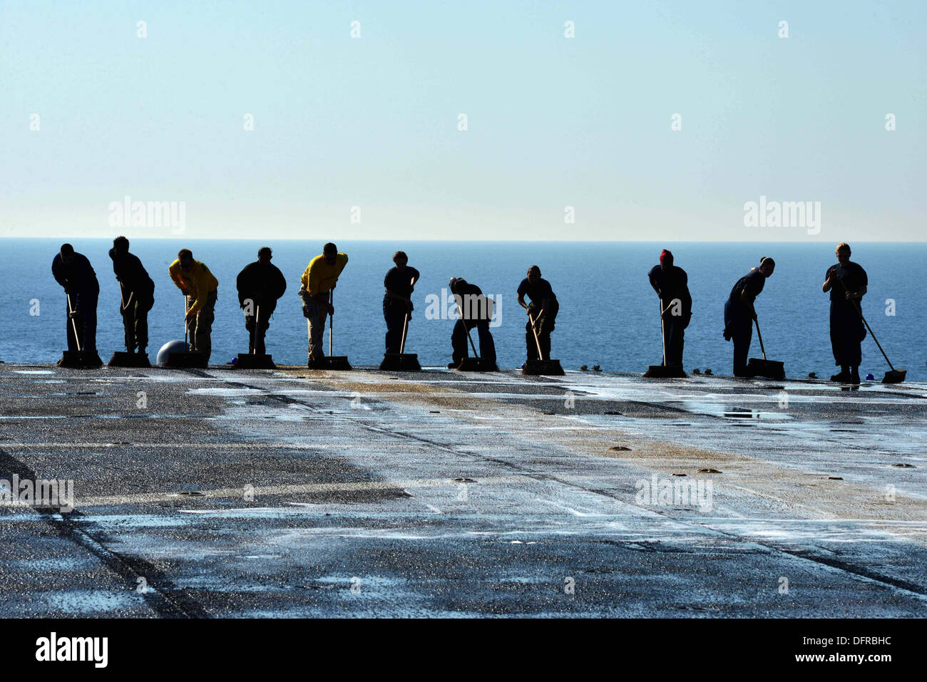Sailors use brooms to clean the deck during a freshwater flight deck ...