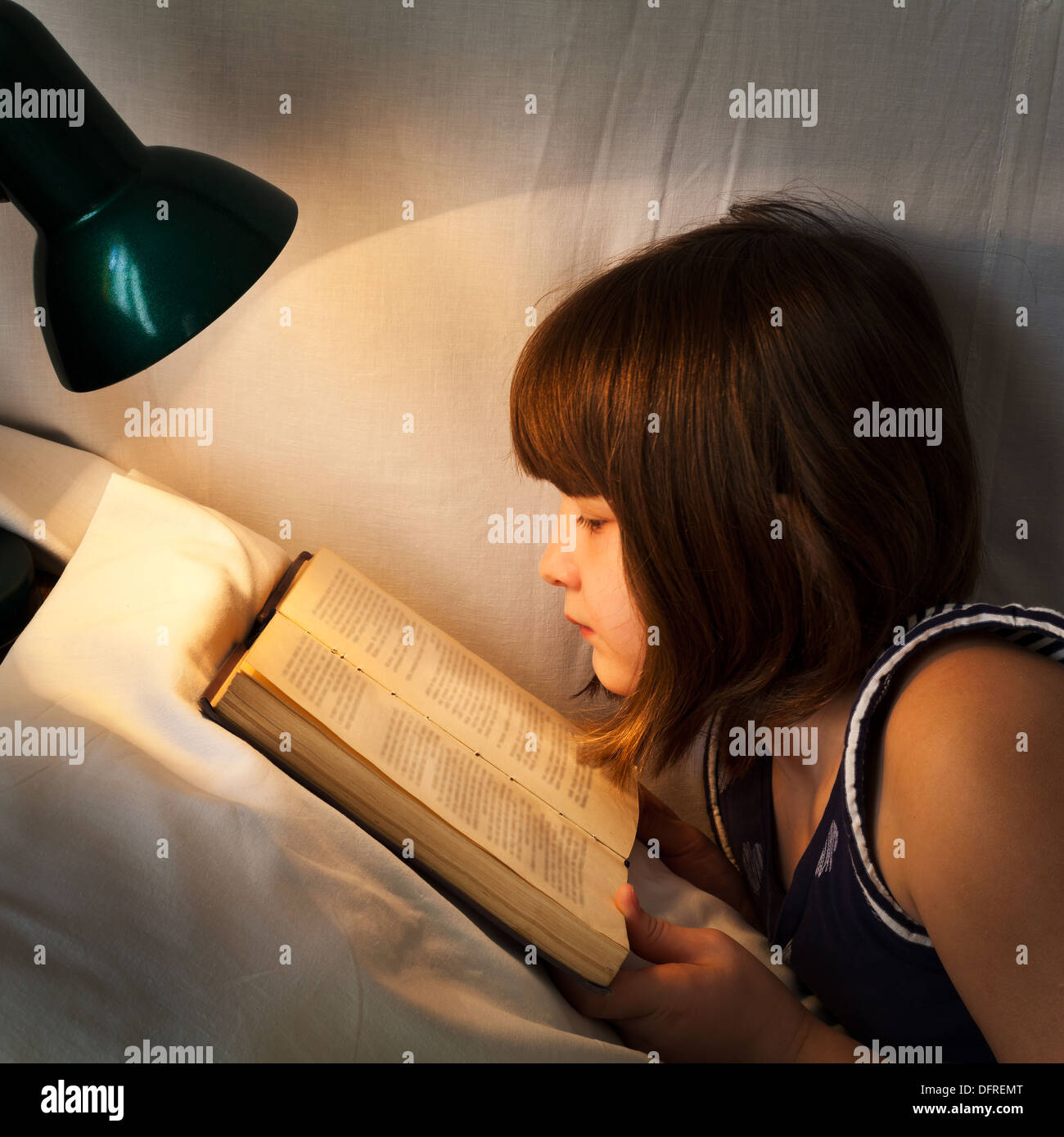 girl reading book on bed at night by light of lamp on bed Stock Photo ...