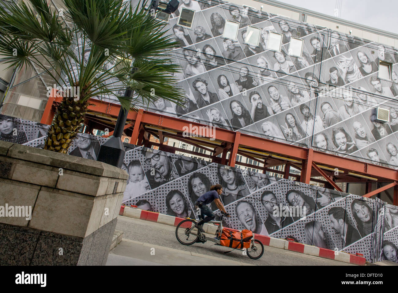 Delivery cyclist pedals past a site office and a construction hoarding ...