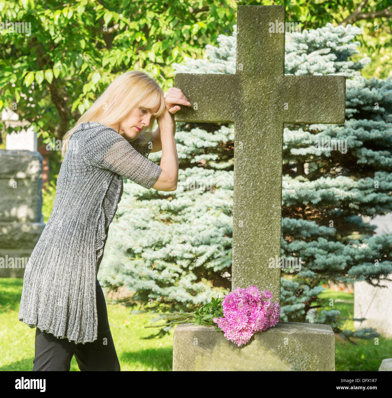 Woman mourns in cemetery resting on cross gravestone Stock Photo - Alamy