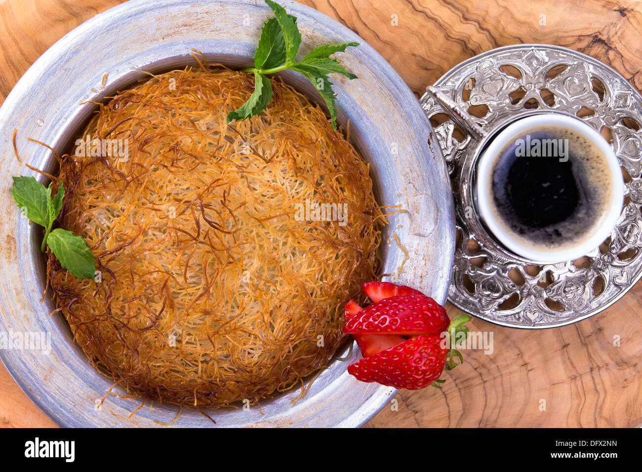 Turkish dessert kunefe isolated on a olive tree table with mints and ...