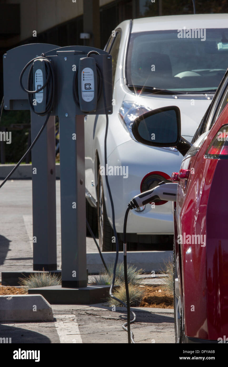 Plug-in electric cars plugged into EV charging stations to charge their ...