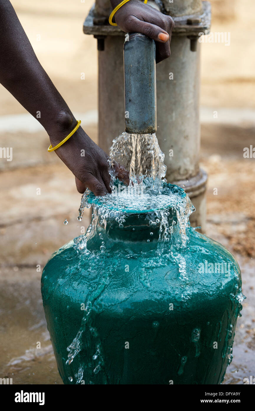 Rural indian woman filling plastic water pot from a rural water pump ...