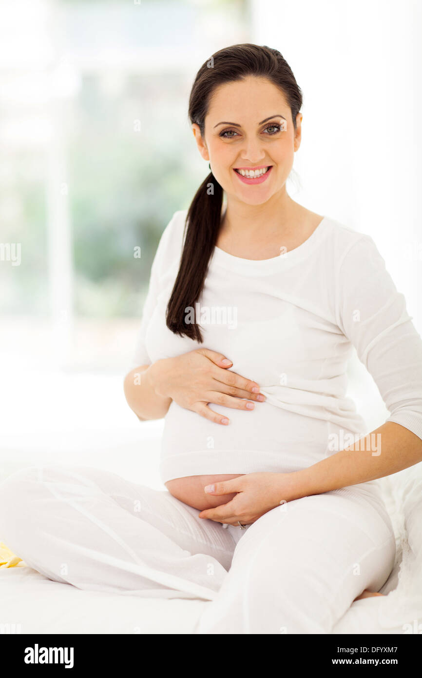 Attractive Pregnant Woman Touching Her Belly While Sitting On A Bed At