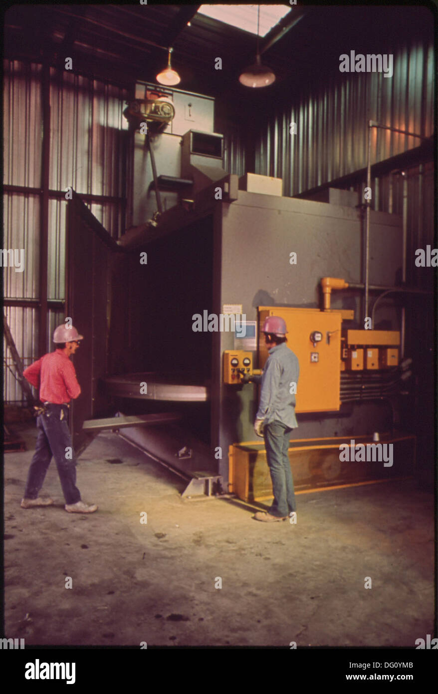 This image shows workers controlling a large enclosed sandblasting unit ...