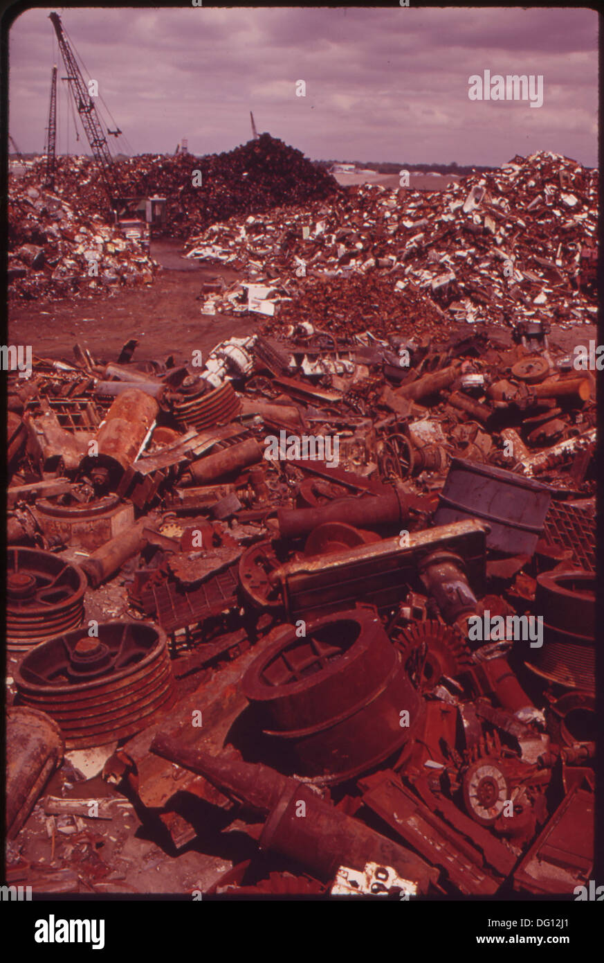 This image depicts a scrap metal yard located on a waterfront. The yard ...