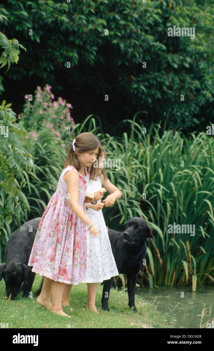 Two small girls wearing dresses standing with two black Labrador dogs ...
